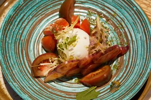Um prato com uma salada, um tomate e um pedaço de carne.