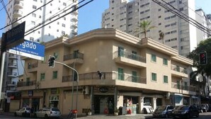 Um edifício de vários andares com varandas, fachada comercial e carros estacionados.