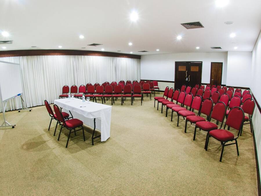 Uma sala de conferências com uma mesa comprida e cadeiras vermelhas, um quadro branco e um projetor.