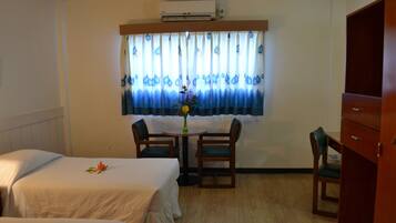 Quarto de hotel com duas camas, uma mesinha com cadeiras, uma janela com cortinas e um aparelho de ar condicionado.