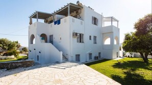 Um edifício moderno e branco, com entrada em pedra, escadaria e um pequeno jardim.