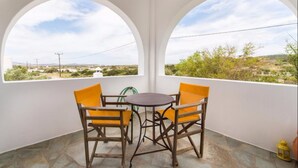 Varanda com duas cadeiras e uma mesa, com vista para uma paisagem rural.