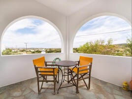Varanda com duas cadeiras e uma mesa, com vista para uma paisagem rural.