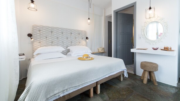 Quarto com cama, mesa de cabeceira, abajur e um banquinho.