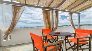 Uma área de estar coberta ao ar livre, com mesa, cadeiras, janelas amplas e vista para a paisagem.