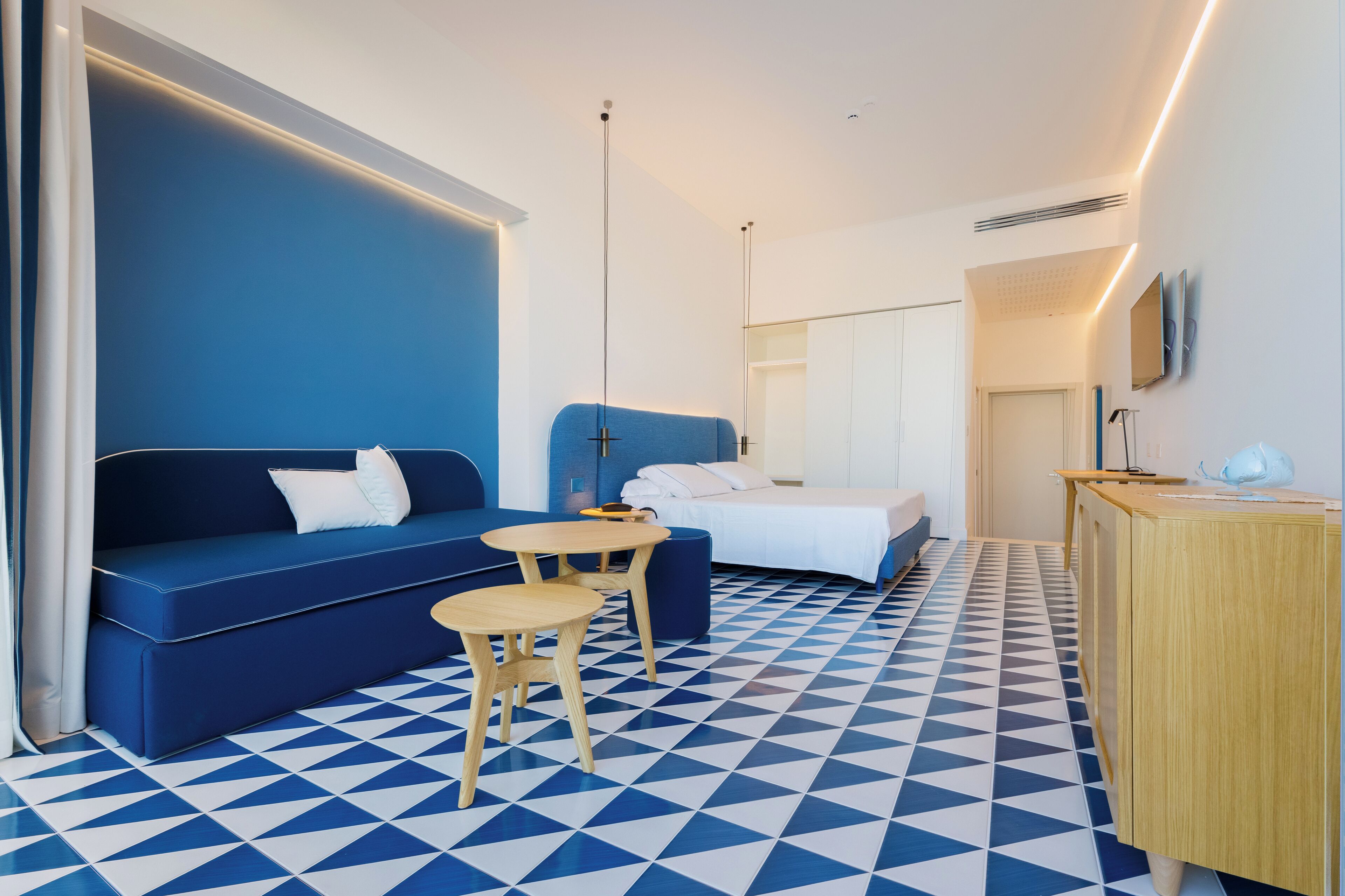 Quarto de hotel moderno com um sofá azul, uma cama, uma pequena mesa de madeira e um armário de madeira.