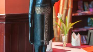 Estátua de uma figura sentada com a mão levantada, possivelmente um símbolo religioso ou cultural, colocada sobre um pedestal.
