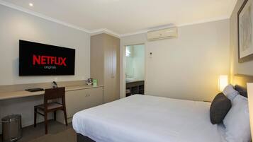 Quarto de hotel com cama, escrivaninha, cadeira, TV exibindo 'NETFLIX originals' e uma lixeira.