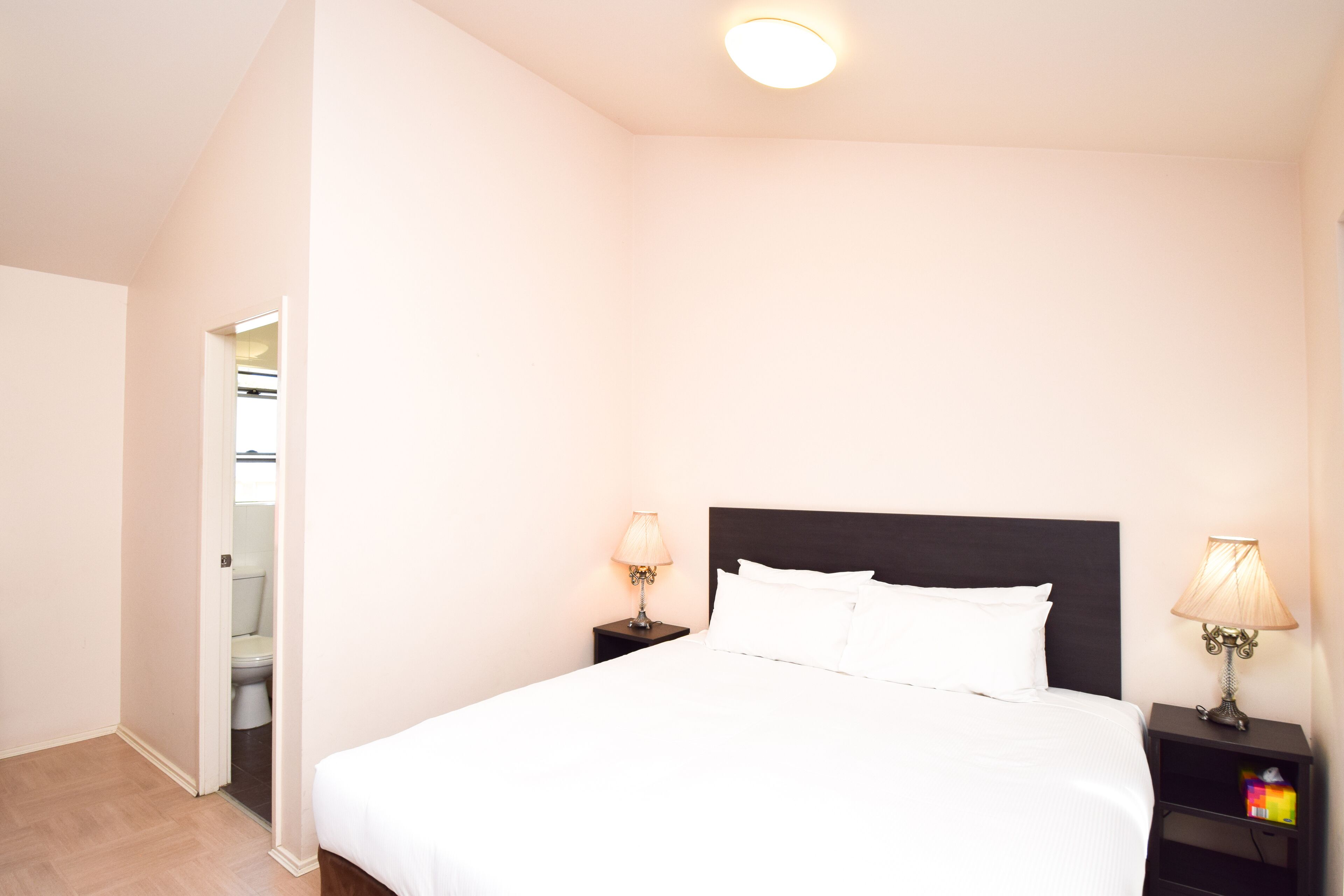Quarto com cama, duas mesas de cabeceira com abajures, um criado-mudo e um armário.