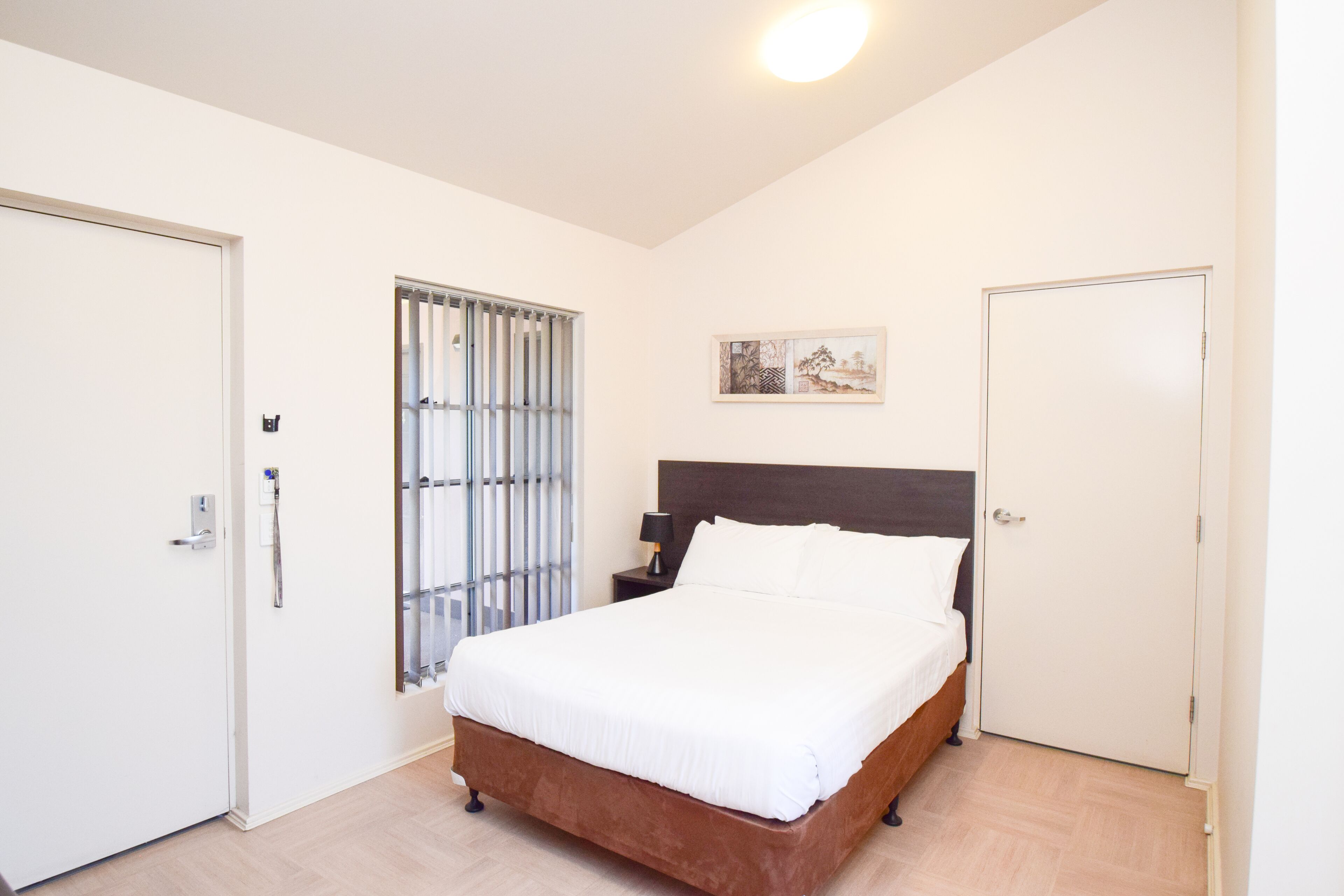 Um quarto com uma cama, uma mesa de cabeceira, uma janela com persianas e uma porta.