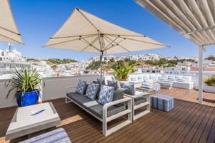 Terraço no telhado com um conjunto de sofás, uma mesa e um grande guarda-sol.