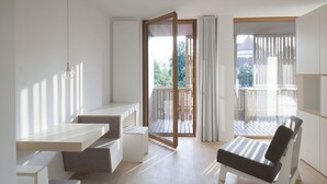 Quarto moderno, bem iluminado, com varanda, um sofá e uma mesa de jantar.
