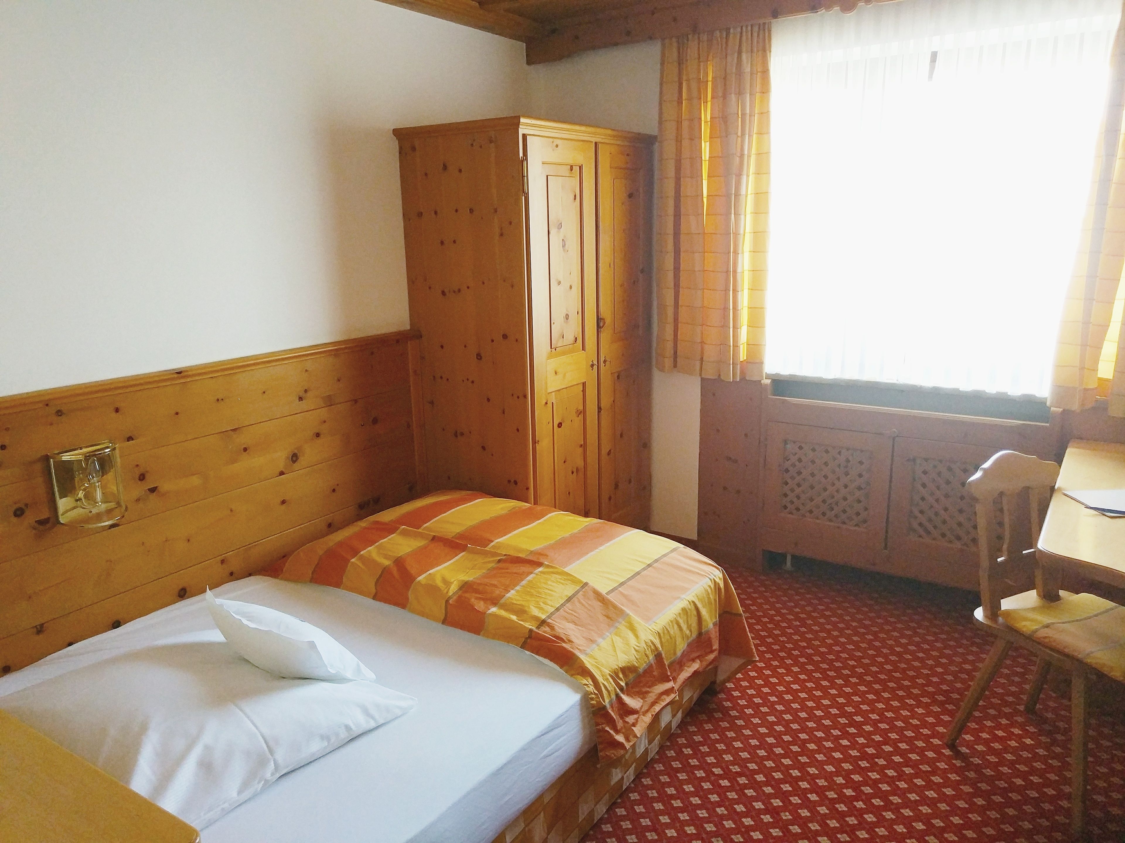 Quarto com uma cama, guarda-roupa de madeira, secretária e uma cadeira.