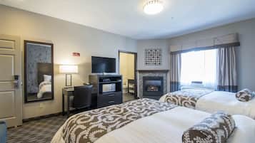 Quarto de hotel com duas camas, televisão, lareira e secretária com abajur.