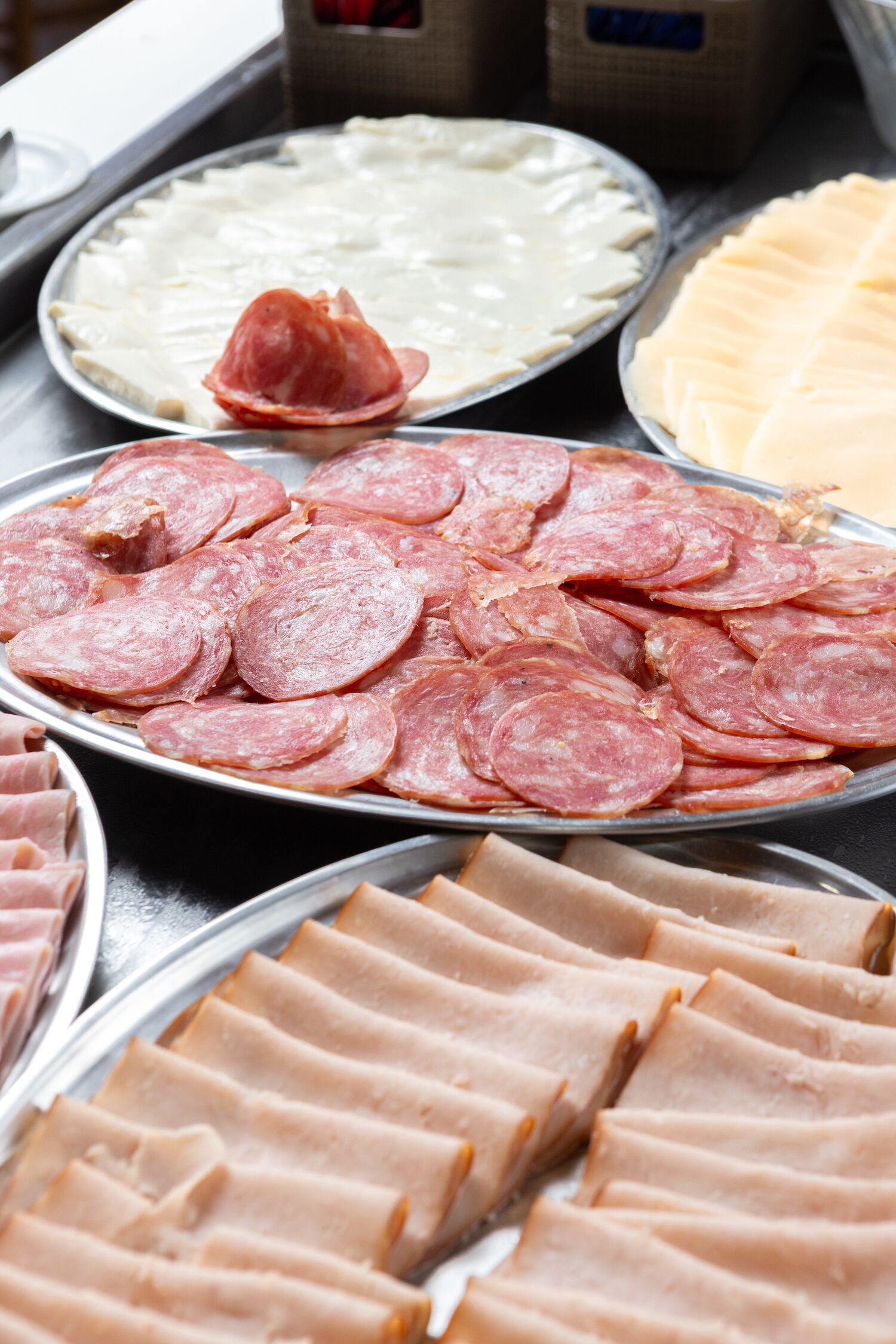 Diversos tipos de carne fatiada em uma bandeja, incluindo presunto, salame e possivelmente presunto cru.