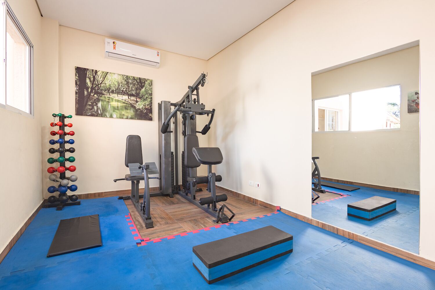 Uma academia com equipamentos de exercícios, tapetes azuis e um espelho.