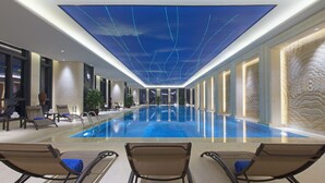 Piscina interior moderna com espreguiçadeiras e teto com desenhos luminosos.