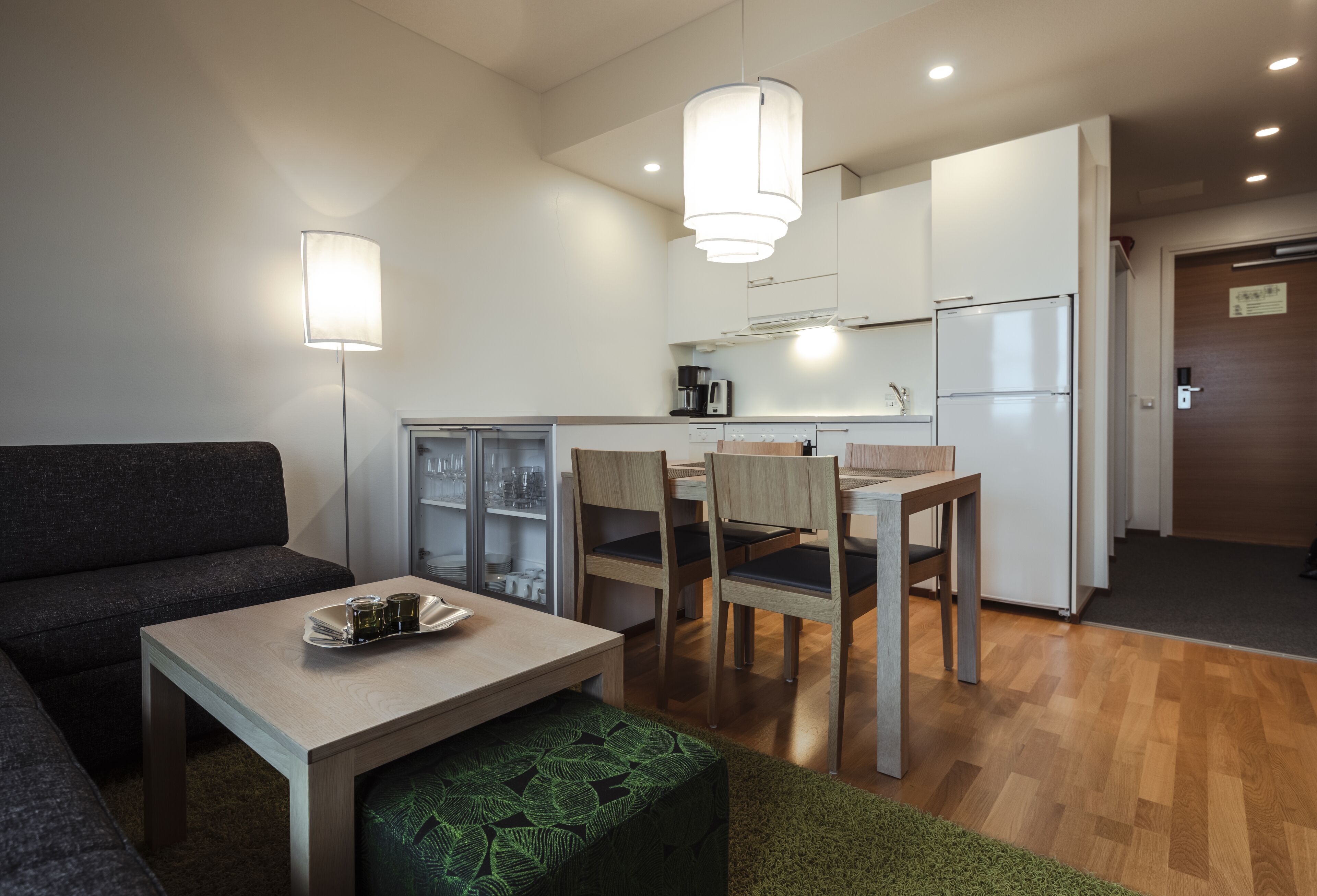 Espaço compacto com sofá, mesa de jantar com cadeiras, cozinha compacta e geladeira.