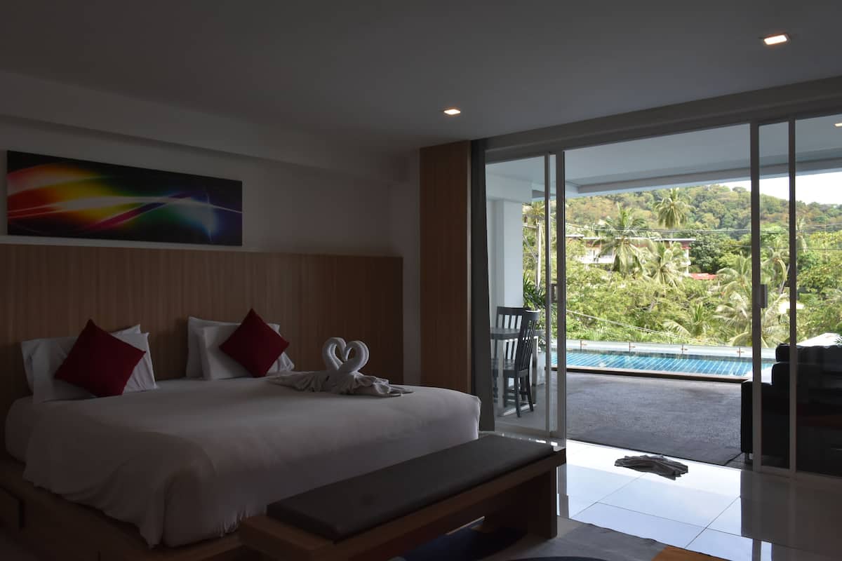 Quarto de hotel com uma cama grande, um banco, uma pintura e vista para uma piscina e áreas verdes.