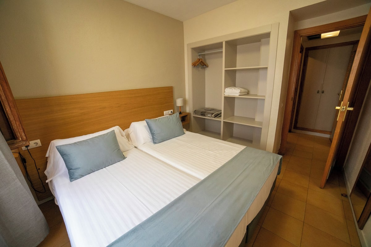 Quarto de hotel com uma cama grande, um guarda-roupa e uma porta que dá para outro cômodo.