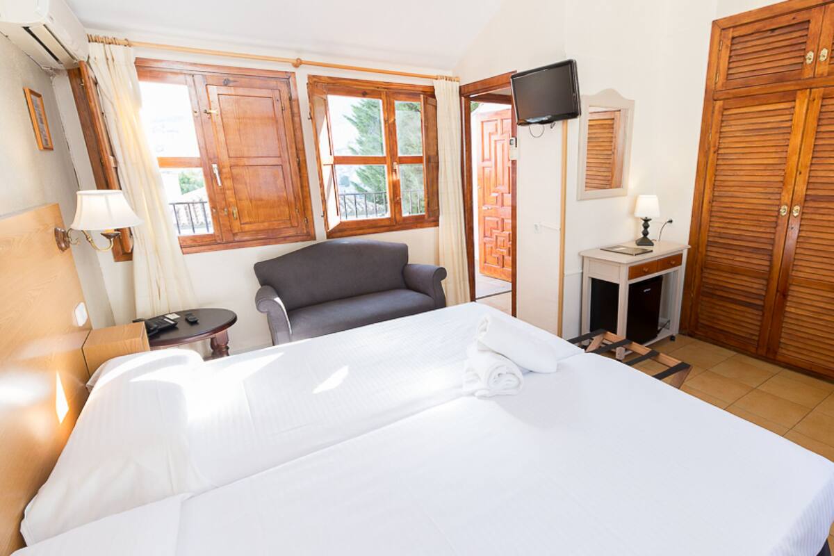 Quarto de hotel com cama, secretária, cadeira, televisão e guarda-roupa.