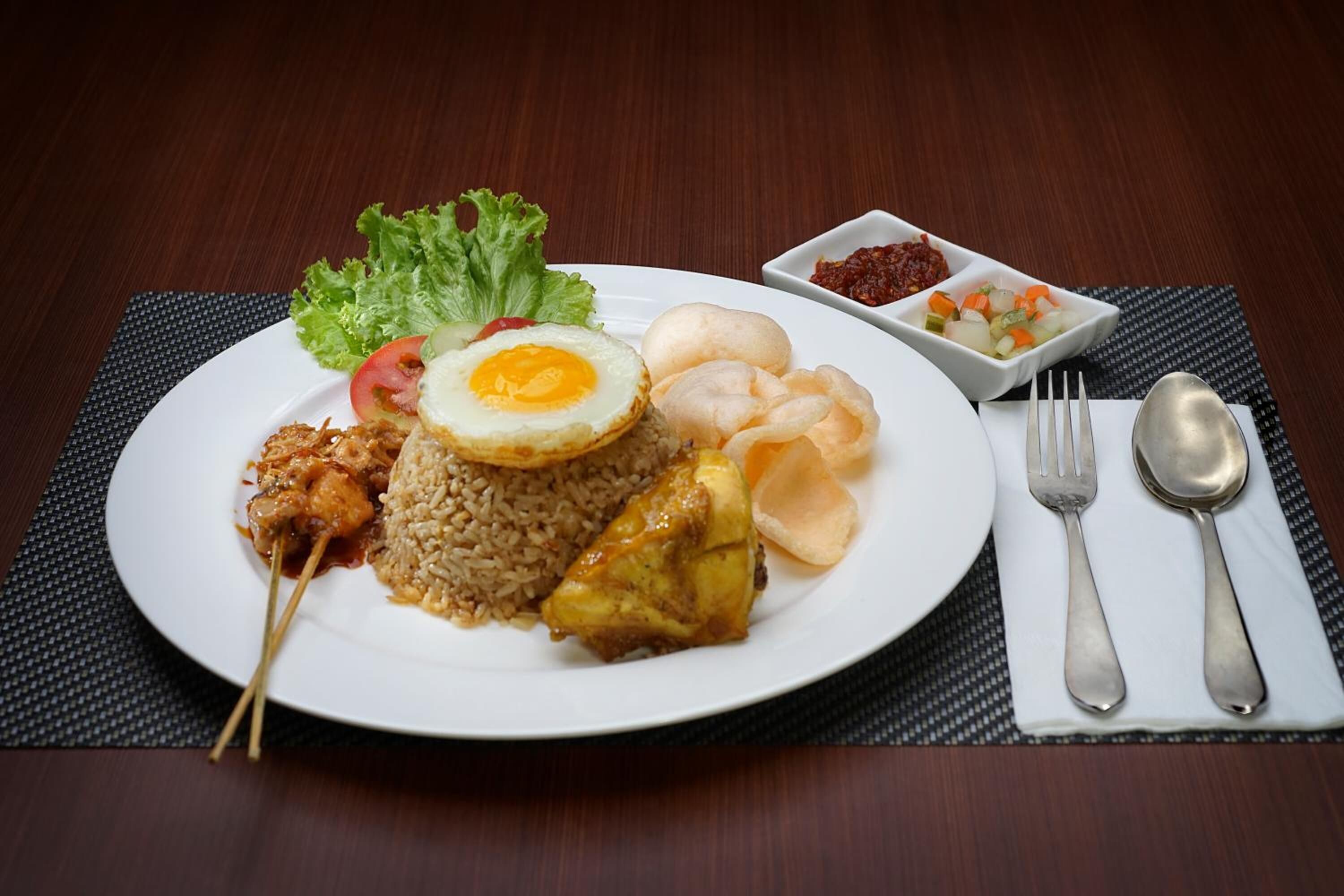 Um prato de comida com arroz, frango e um ovo frito sobre uma mesa de madeira escura.