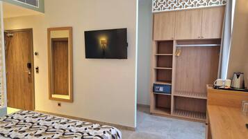 Quarto de hotel com cama, televisão, guarda-roupa e escrivaninha com chaleira e chávenas.