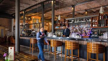 Uma área de bar com banquetas de madeira, um bartender e um balcão de bar bem abastecido.