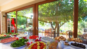Mesa de buffet com diversos alimentos e vista para área externa com mesas e cadeiras.