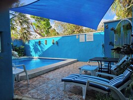 Uma área de piscina com parede azul, cadeiras de descanso e uma mesa.