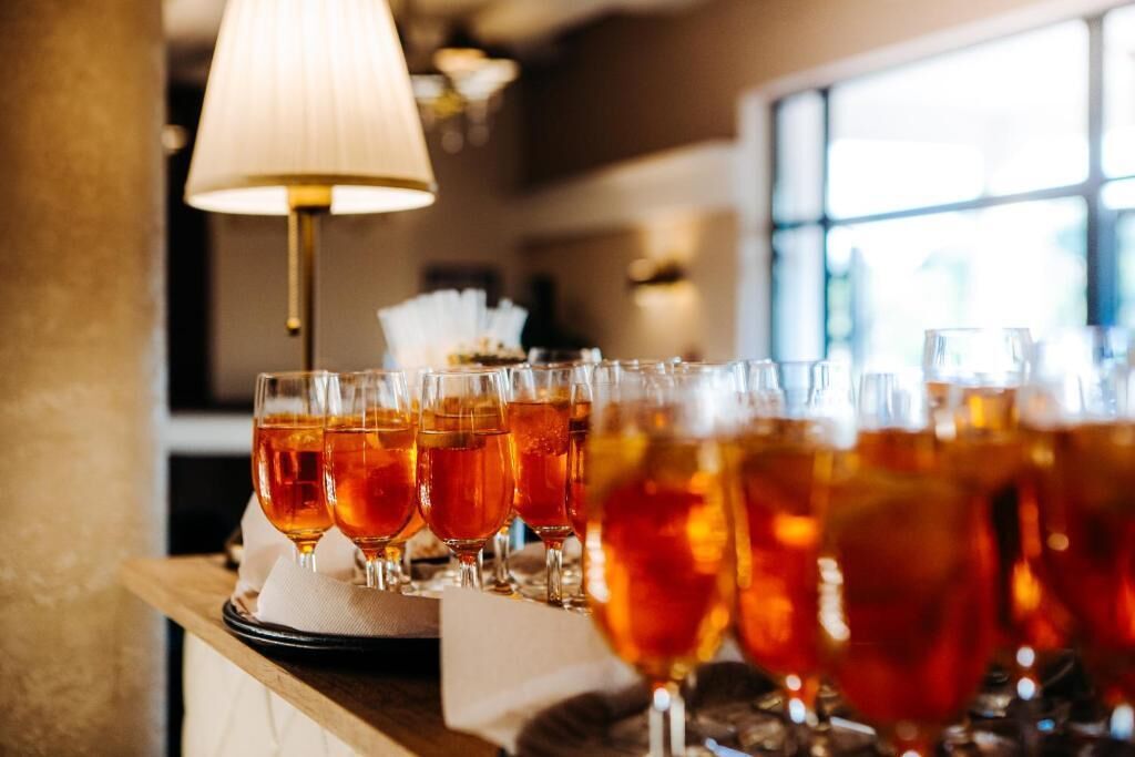 Bar com vários copos de bebidas âmbar, uma lâmpada e uma janela ao fundo.