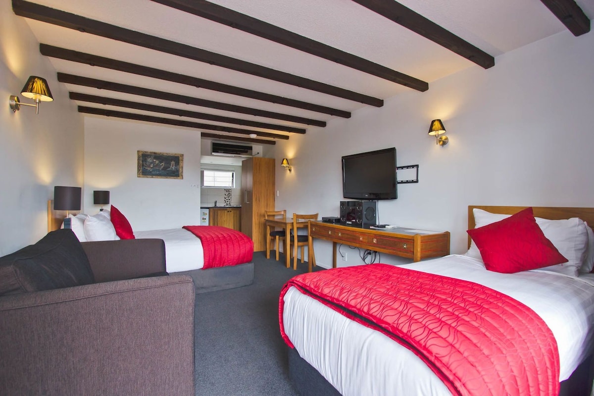 Quarto de hotel com duas camas, uma mesa, televisão e cozinha compacta.