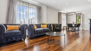 Uma sala de estar moderna com um sofá cinza escuro, uma mesa de centro redonda e uma área de jantar com mesa e cadeiras.