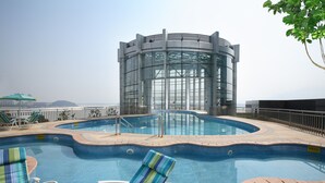 Piscina com espreguiçadeiras e um edifício moderno ao fundo.