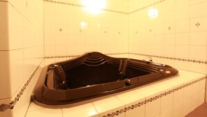 Uma grande banheira de hidromassagem preta em um banheiro com paredes de azulejos brancos e uma borda decorativa.