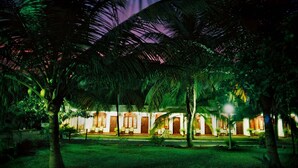 Um edifício com fachada simétrica, grandes janelas e um gramado bem cuidado com palmeiras.