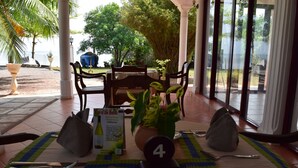 Mesa posta para quatro com vista para o mar, área de estar coberta ao ar livre e um jardim tropical.
