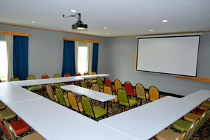 Uma sala de conferência com uma mesa comprida, fileiras de cadeiras, um projetor e uma tela em branco.