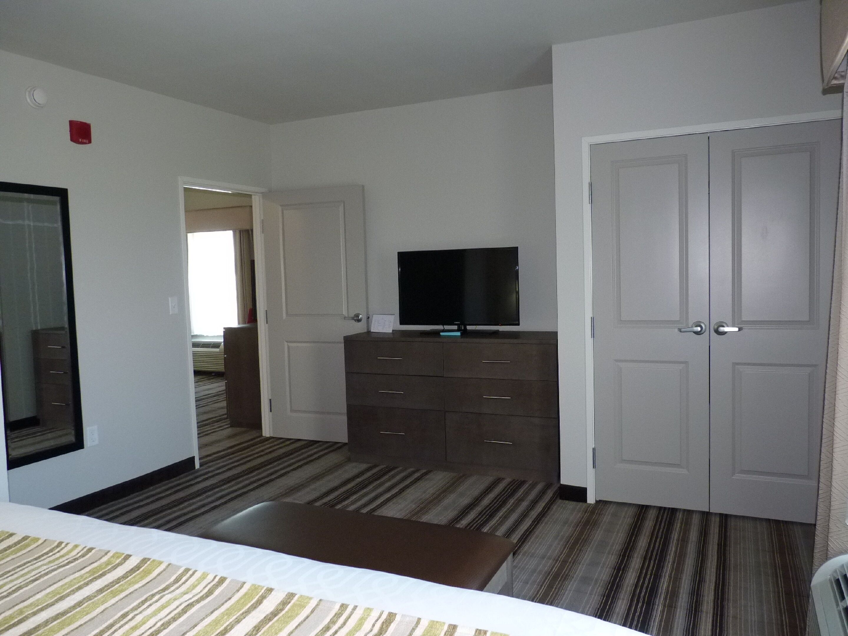 Um quarto de hotel com cama, penteadeira, televisão e porta.