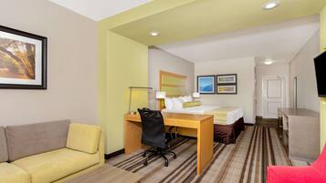 Quarto de hotel com cama, escrivaninha, cadeira, sofá e televisão.