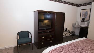 Quarto de hotel com cama, televisão, pequena escrivaninha, cadeira e guarda-roupa.