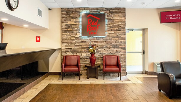 Área de recepção do Red Roof Inn com parede de pedra, duas poltronas de couro, um relógio e placa indicando Wi-Fi gratuito em todos os quartos.