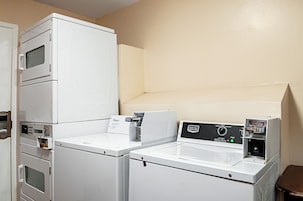 Uma lavanderia com máquinas de lavar e secar empilhadas, uma secadora Maytag e uma secadora Whirlpool.