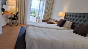 Quarto de hotel com duas camas, uma escrivaninha com cadeira, televisão e vista para o exterior.