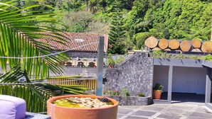 Terraço com parede de pedra, telhado de azulejos e vista para uma encosta arborizada.
