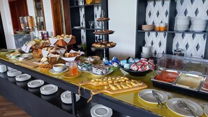 Disposição de buffet com diversos alimentos, incluindo pão, doces e produtos lácteos.