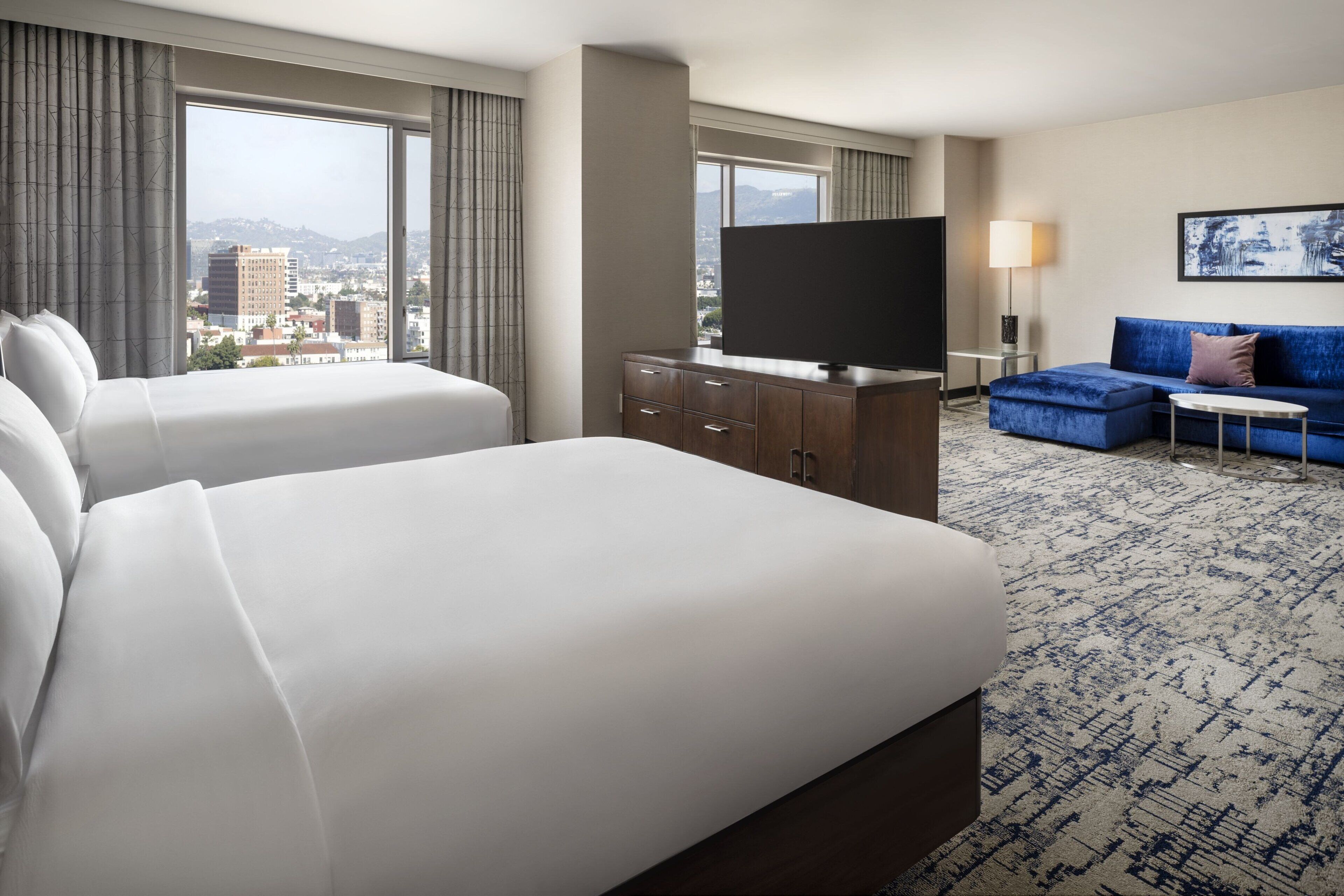 Quarto de hotel com duas camas, uma televisão de tela plana, um sofá e vista para a cidade.