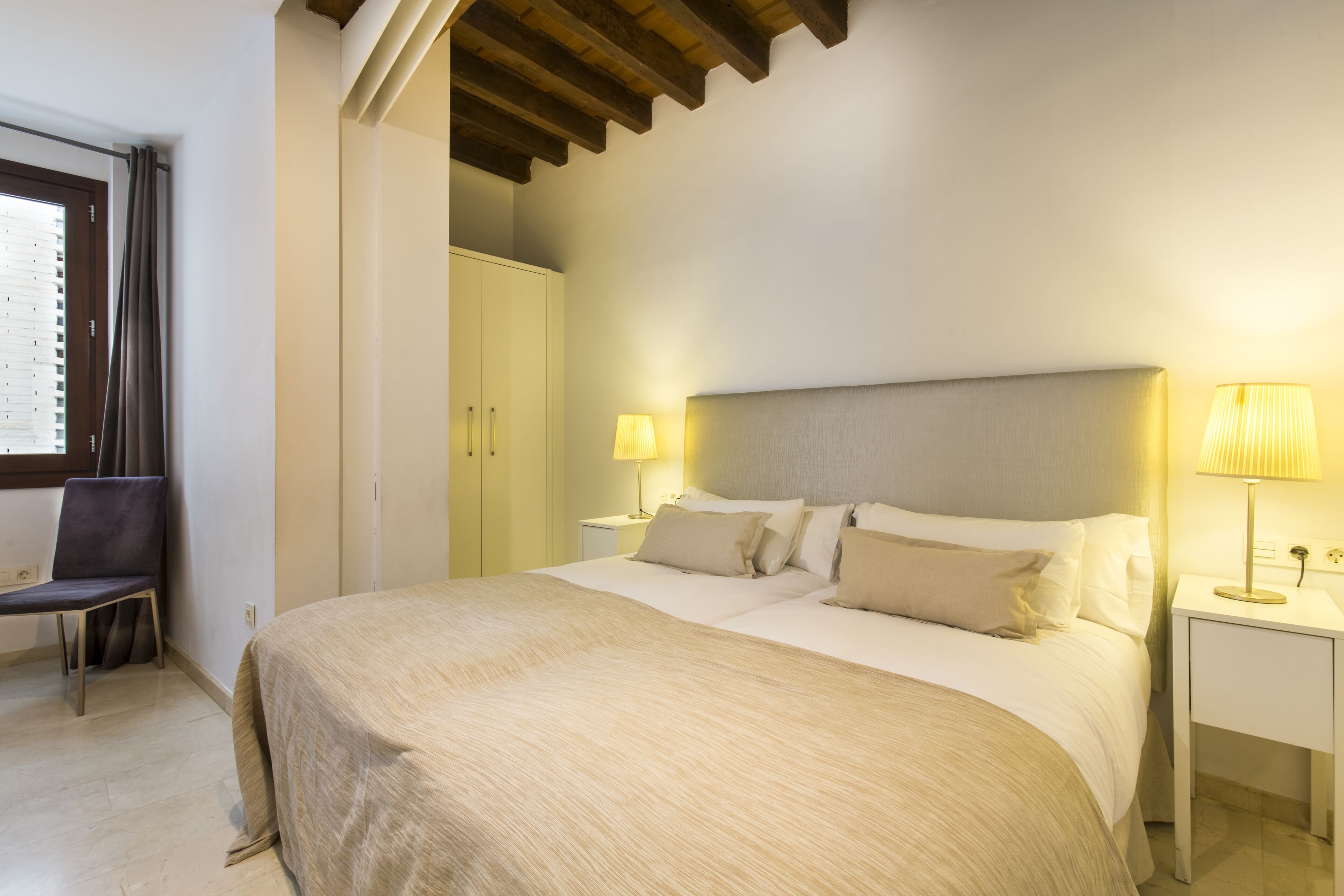 Quarto com cama, luminárias de cabeceira, uma cadeira e um guarda-roupa.