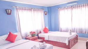 Quarto de hotel com duas camas, cada uma com roupa de cama branca e almofadas vermelhas, mesa de cabeceira com um vaso de flores e cómoda de madeira.