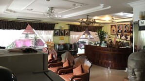 Uma sala de estar ampla com pé direito alto, um balcão de recepção de madeira e uma área de estar com almofadas estampadas.